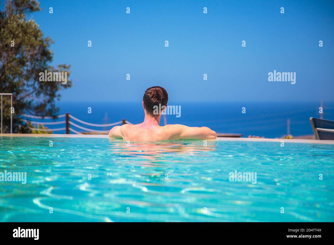 Caucasian young man in the infinity pool watching the ocean view ...