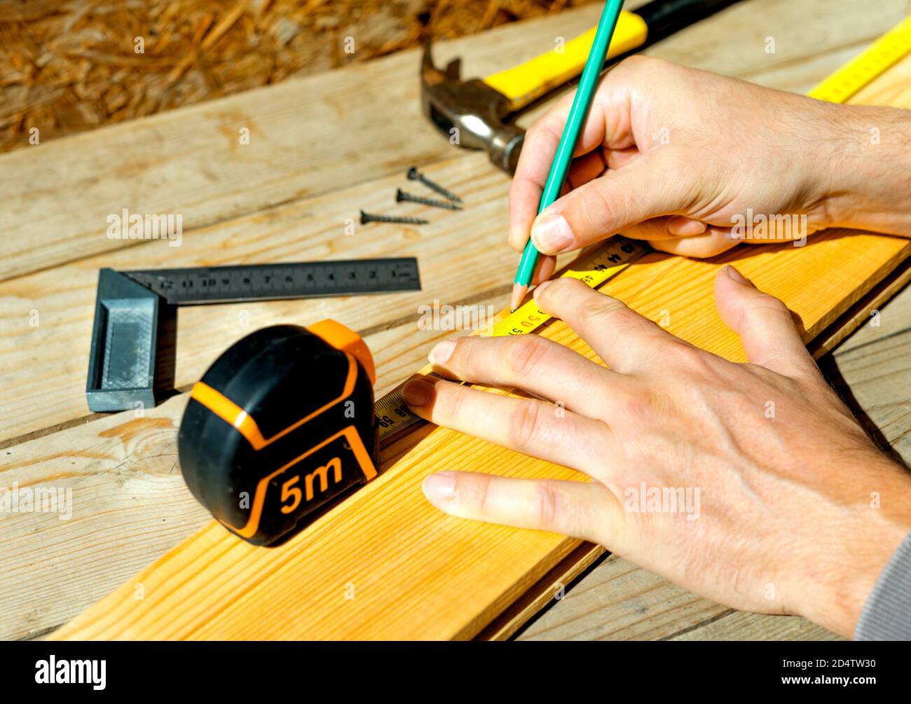 Male carpenter notes with pencil using measuring tape on the board ...