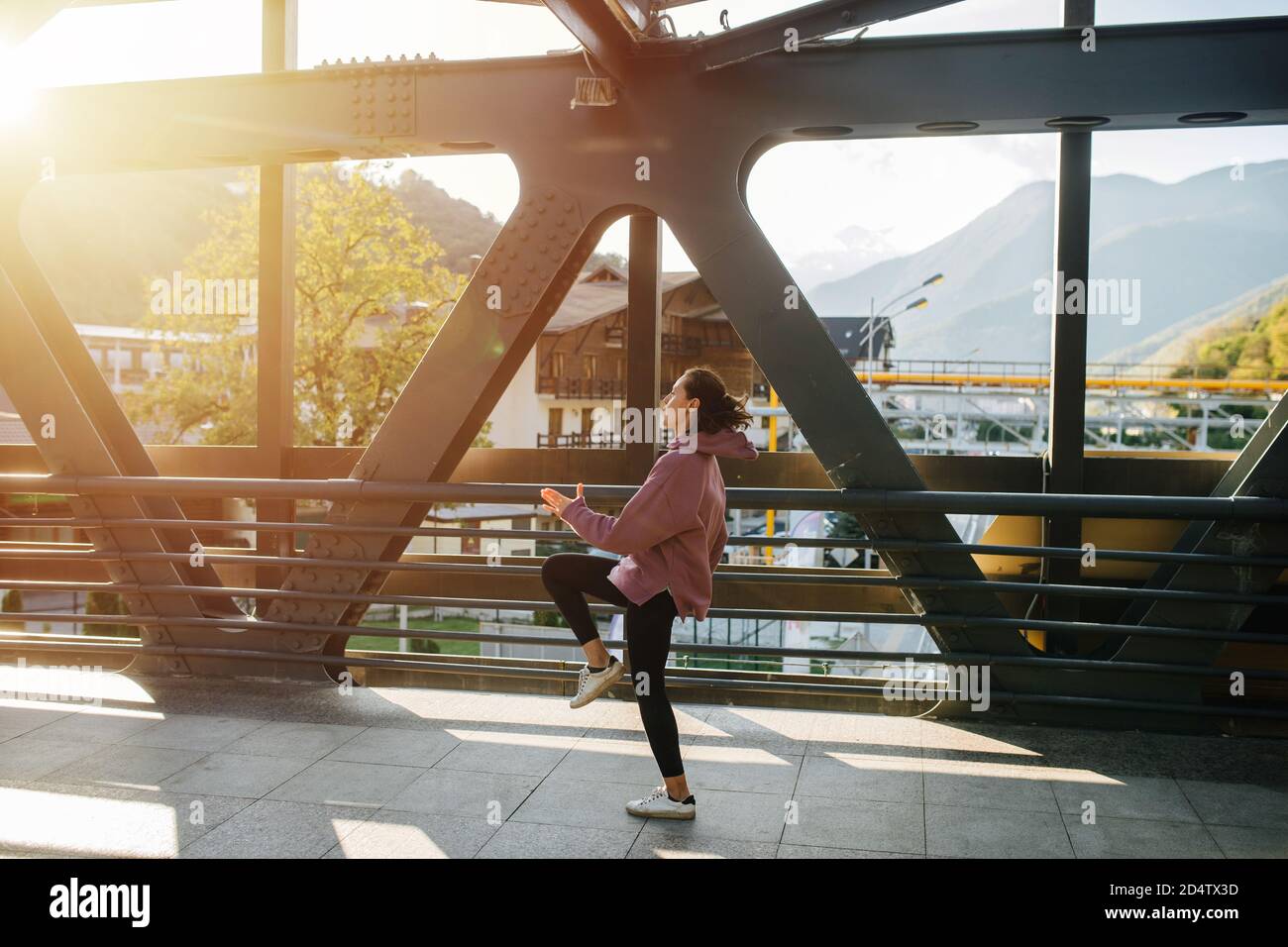 Willful young woman exercising on a steel girder walking bridge. Side ...
