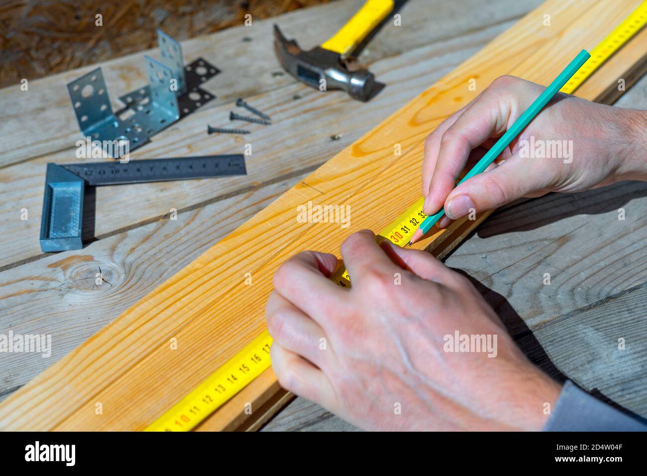 Male carpenter notes with pencil using measuring tape on the board ...