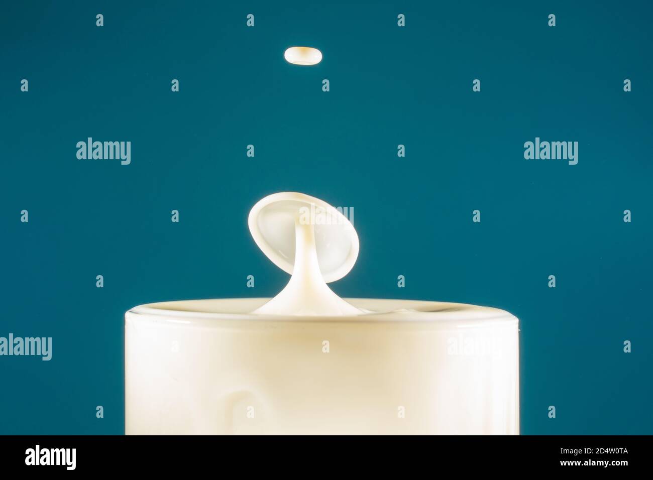 Two drops of milk fall into the long drink glass hitting each other ...