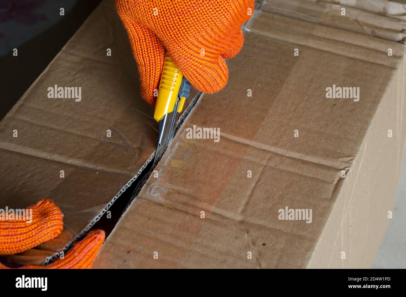 A worker wearing protective gloves opens a cardboard box. A hand with a ...