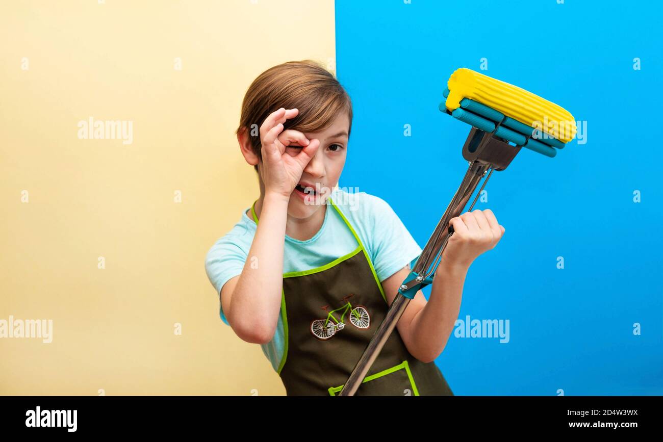 The boy helps to clean up. Photo of a cheerful and happy boy with a mop ...