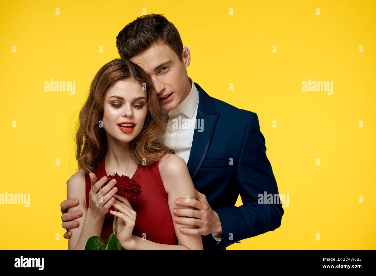 A romantic man hugs a woman in a red dress with a rose in his hand on a ...