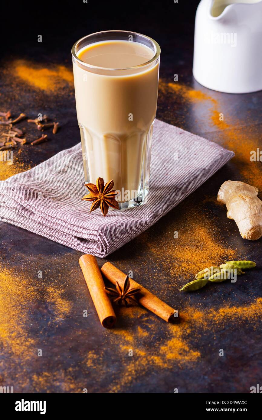 Glass of masala tea and scattered spices. Masala chai tea and milk jug ...