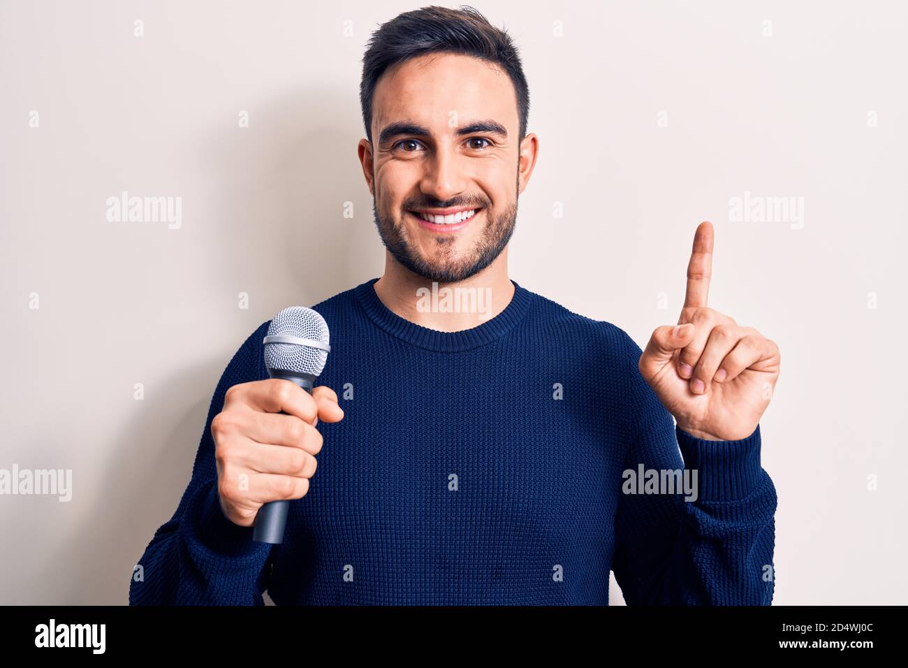 Young handsome singer man with beard singing song using microphone over white background smiling ...