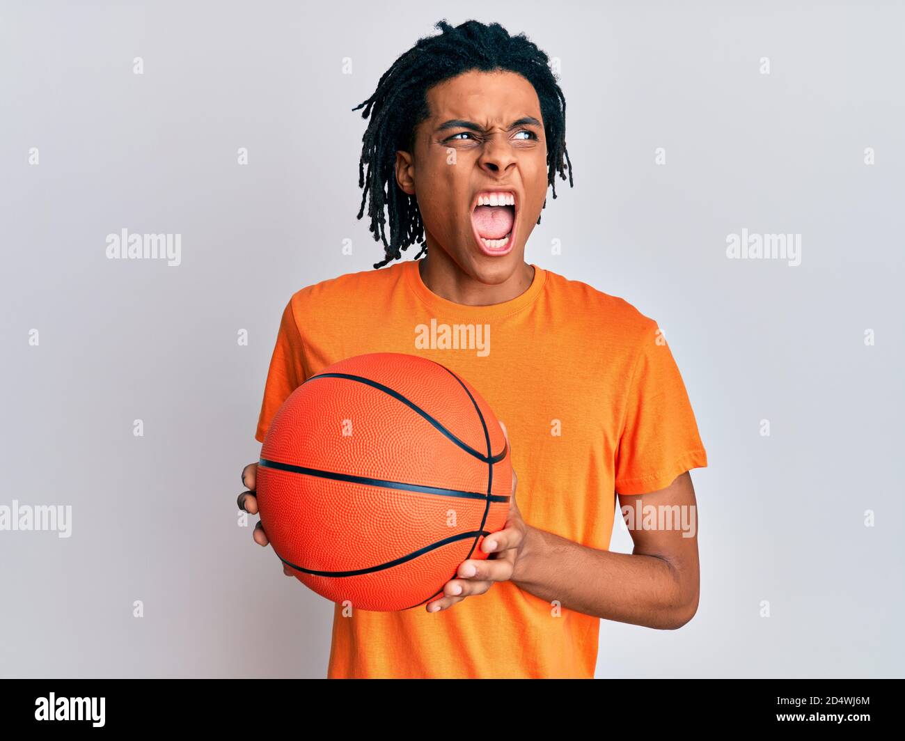 Young african american man holding basketball ball angry and mad ...