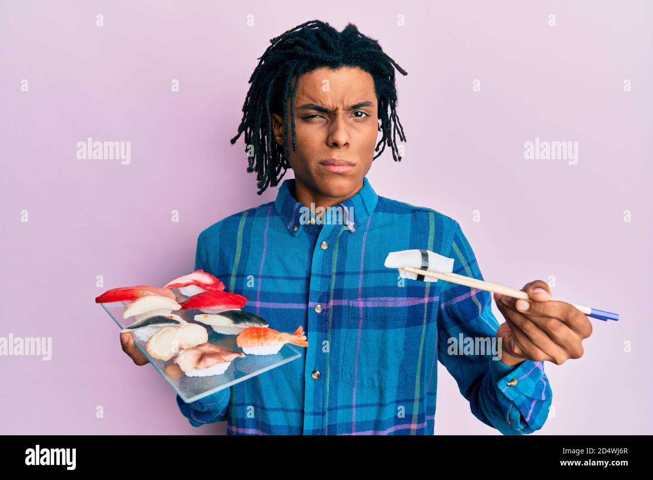Young african american man eating sushi using chopsticks skeptic and ...