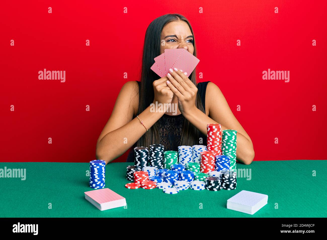 Young hispanic woman playing gambling poker covering face with cards ...