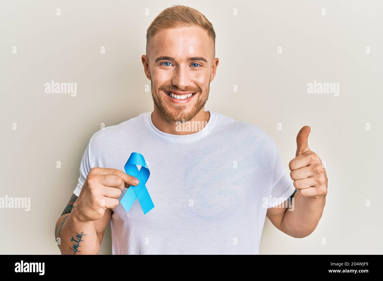 Young caucasian man holding blue ribbon smiling happy and positive ...
