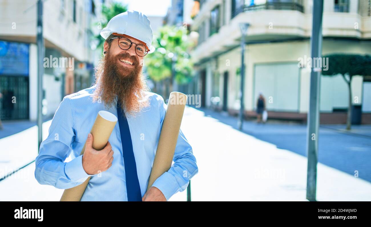 Young redhead architect man with long beard wearing hardhat smiling ...