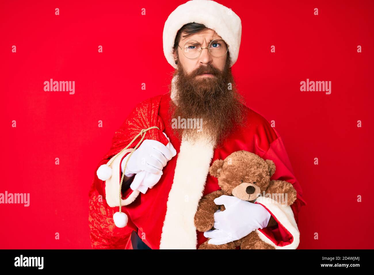 Handsome young red head man with long beard wearing santa claus costume ...