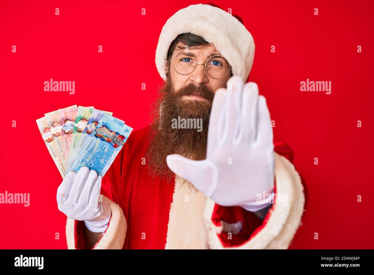 Handsome young red head man with long beard wearing santa claus costume ...