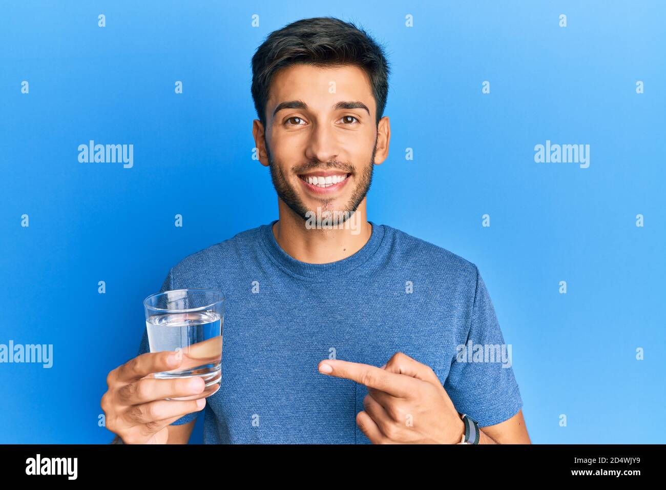 Young handsome man drinking glass of water smiling happy pointing with ...