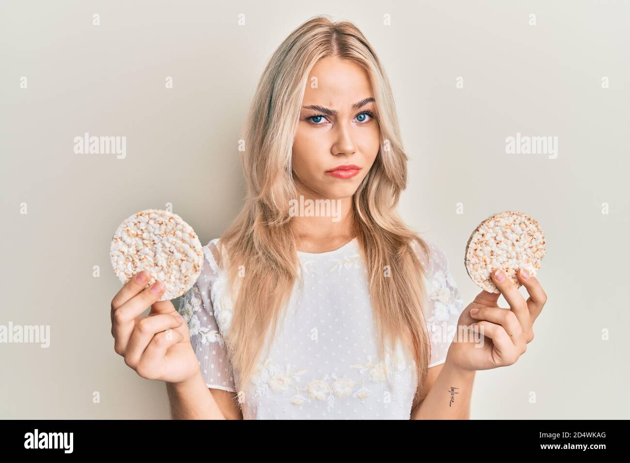 Beautiful caucasian blonde girl eating healthy rice crackers skeptic ...