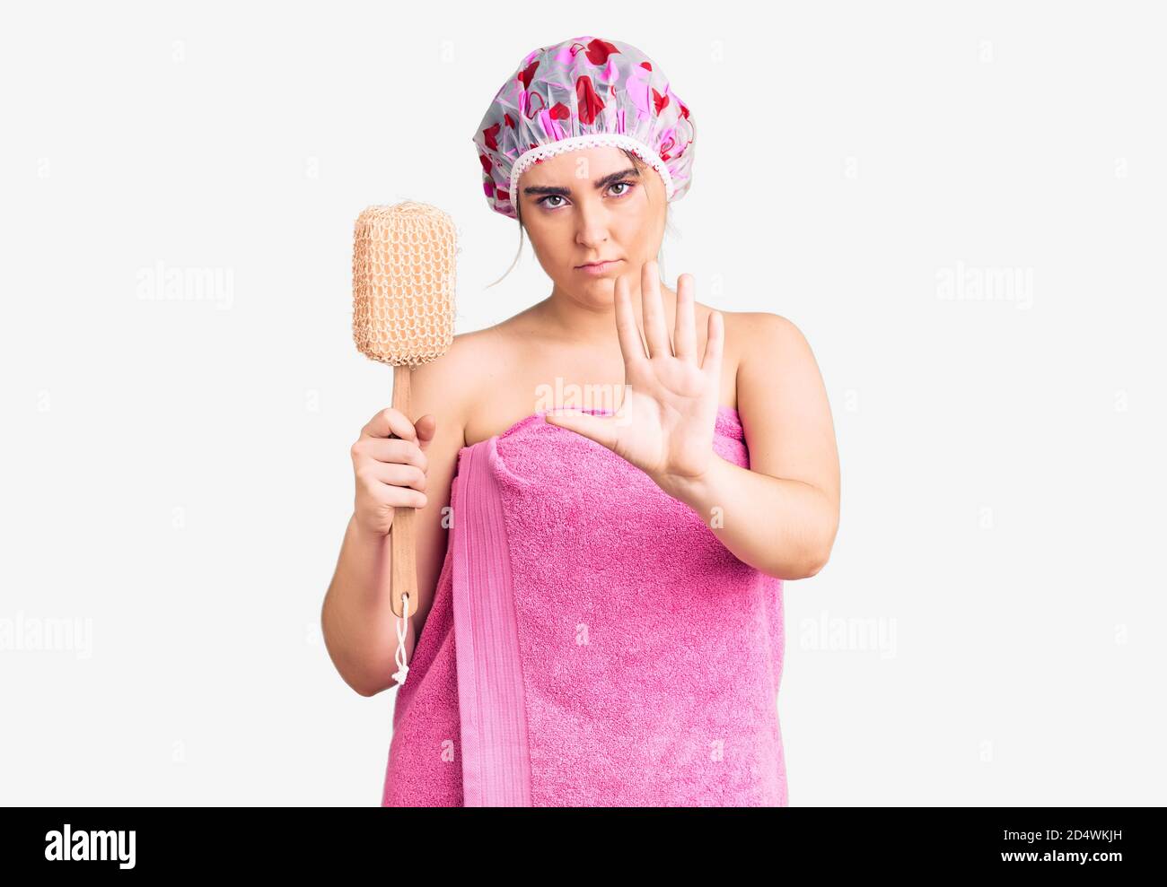 Young caucasian woman wearing shower cap and towel holding sponge with ...