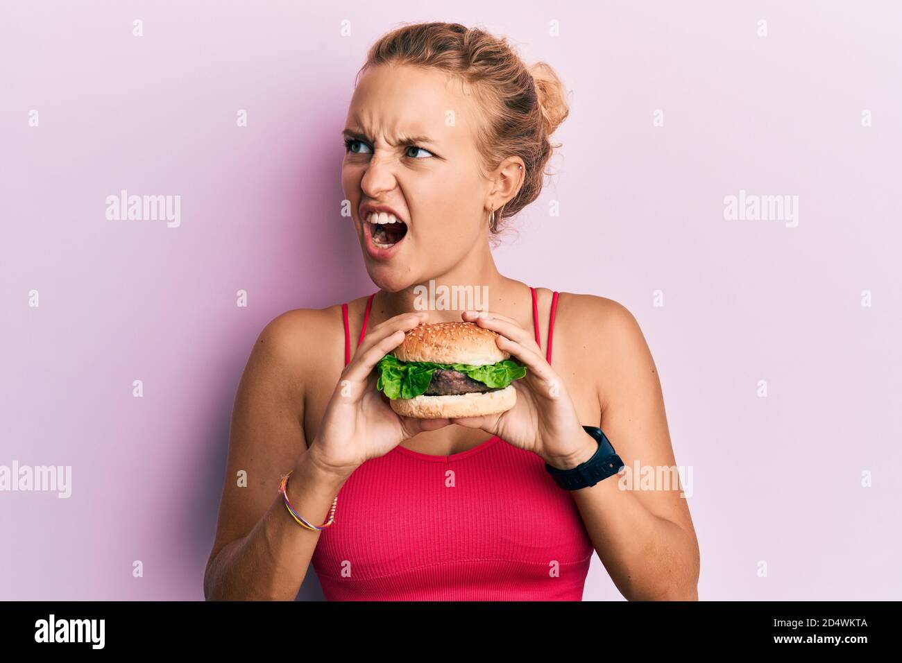 Beautiful caucasian woman eating a tasty classic burger angry and mad ...