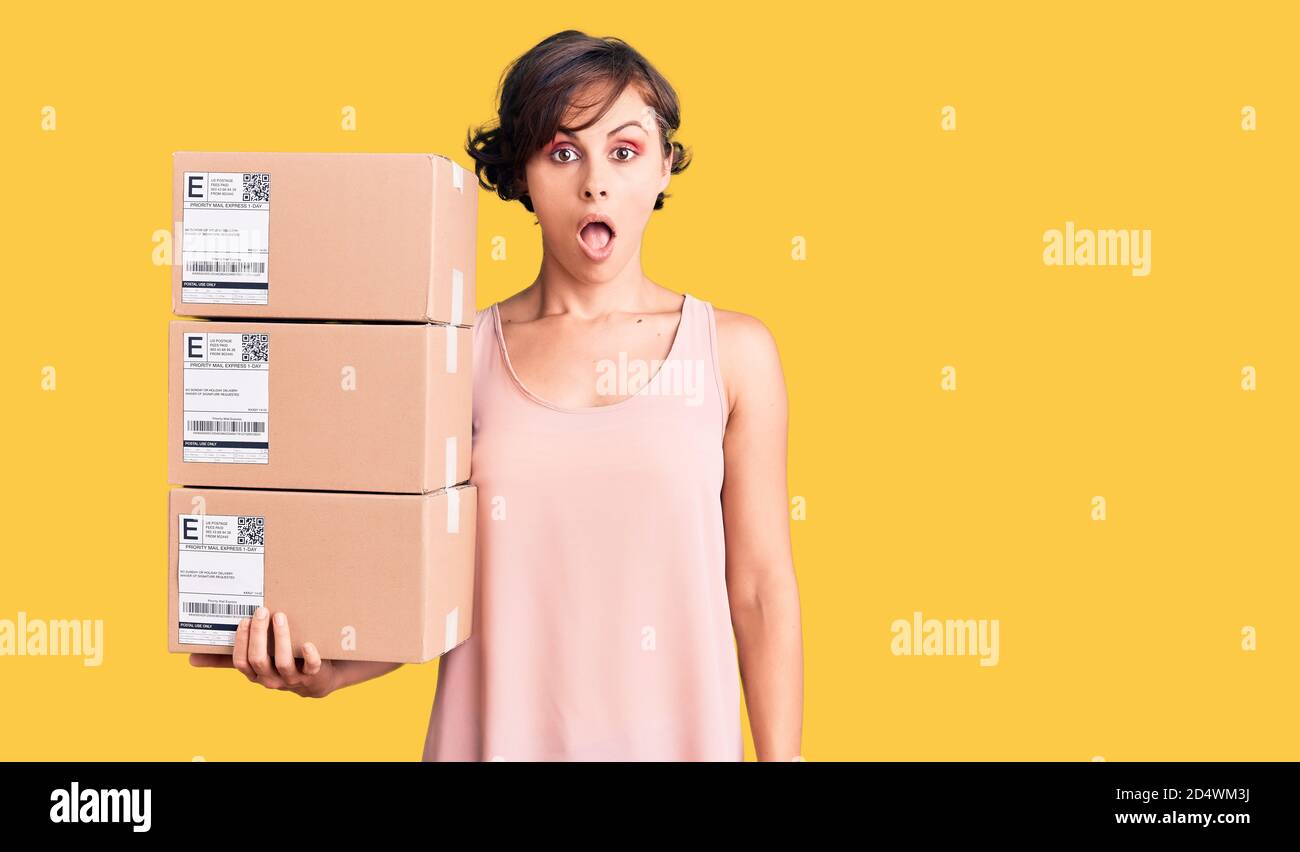 Beautiful young woman with short hair holding delivery packages scared ...
