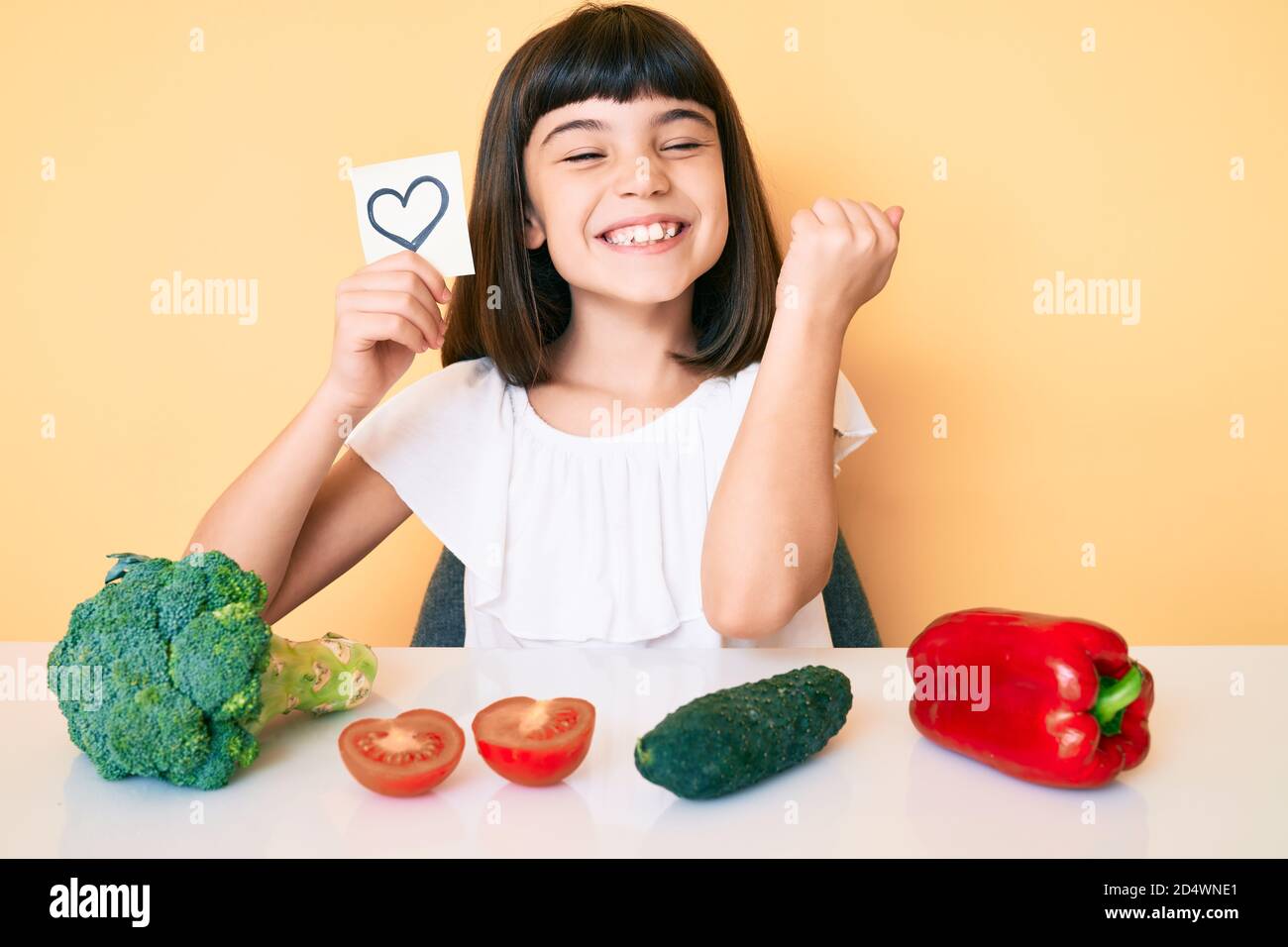 Young little girl with bang sitting on the table with veggies holding ...