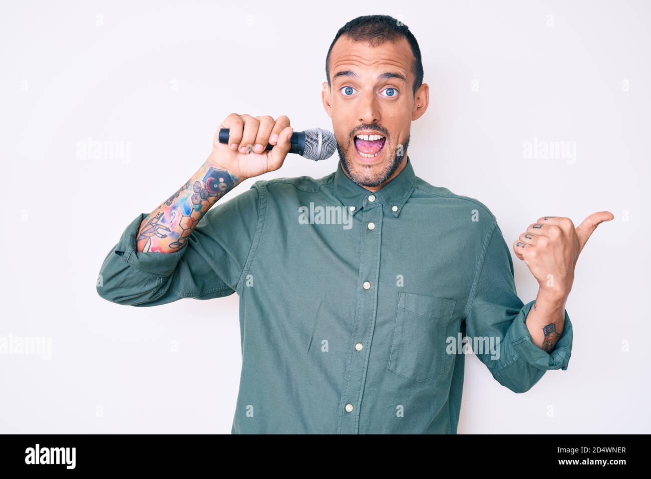 Young handsome man with tattoo singing song using microphone pointing ...
