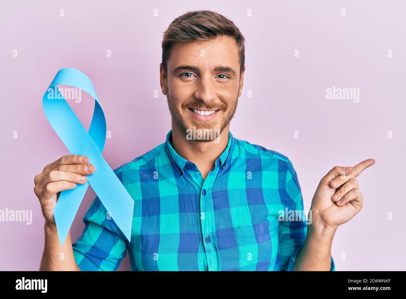 Handsome caucasian man holding blue ribbon smiling happy pointing with ...