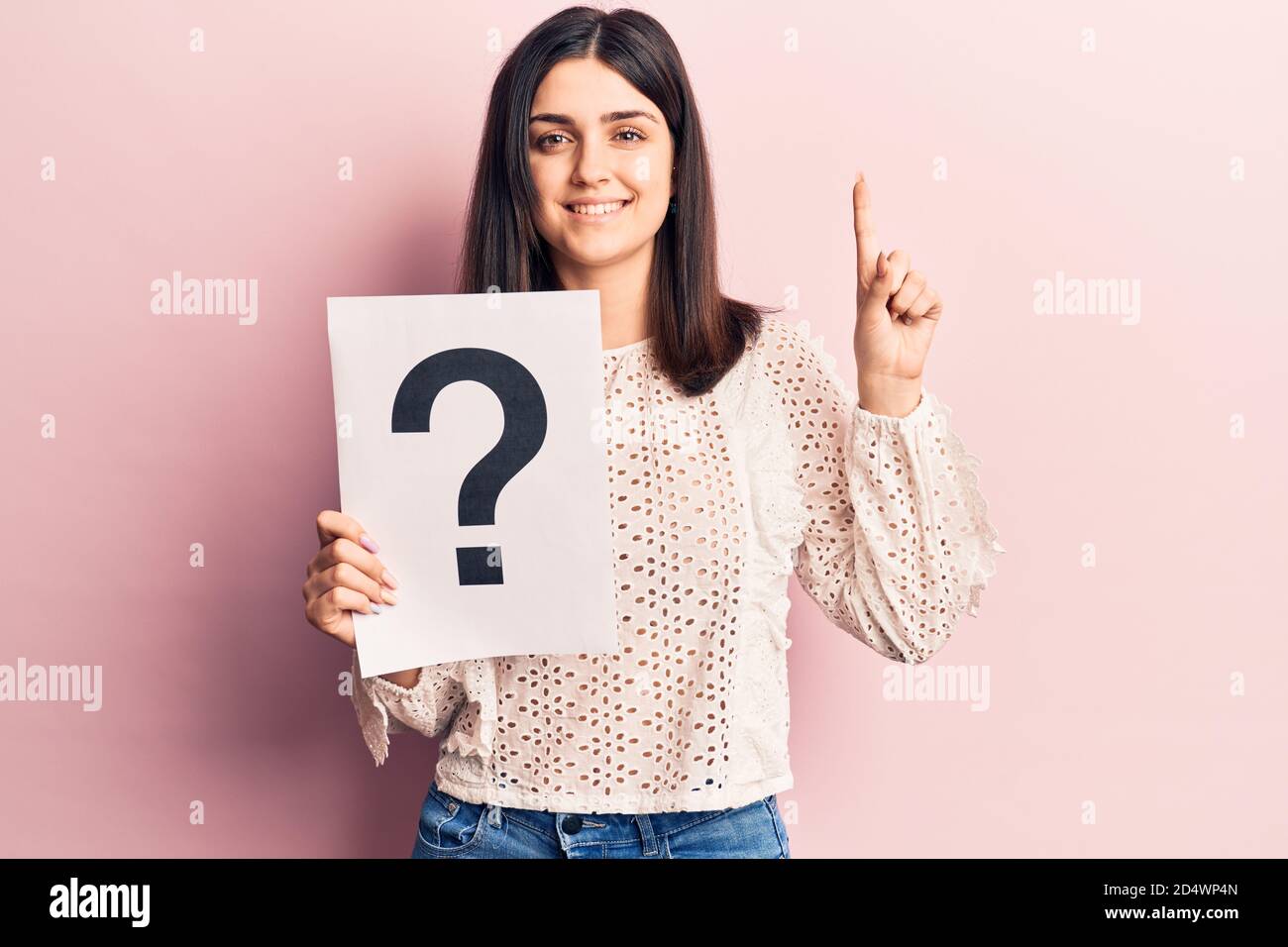 Young beautiful girl holding question mark smiling with an idea or ...