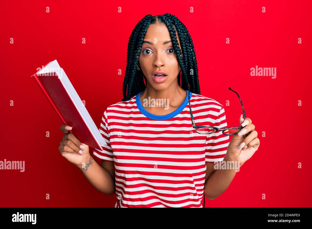 Beautiful hispanic woman reading a book with glasses afraid and shocked ...