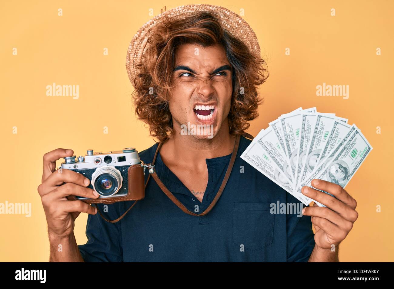 Young hispanic man holding vintage camera and dollars angry and mad ...