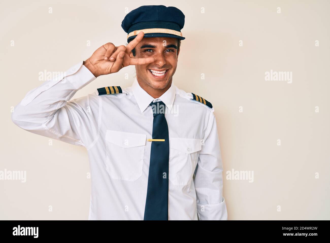 Young hispanic man wearing airplane pilot uniform doing peace symbol ...