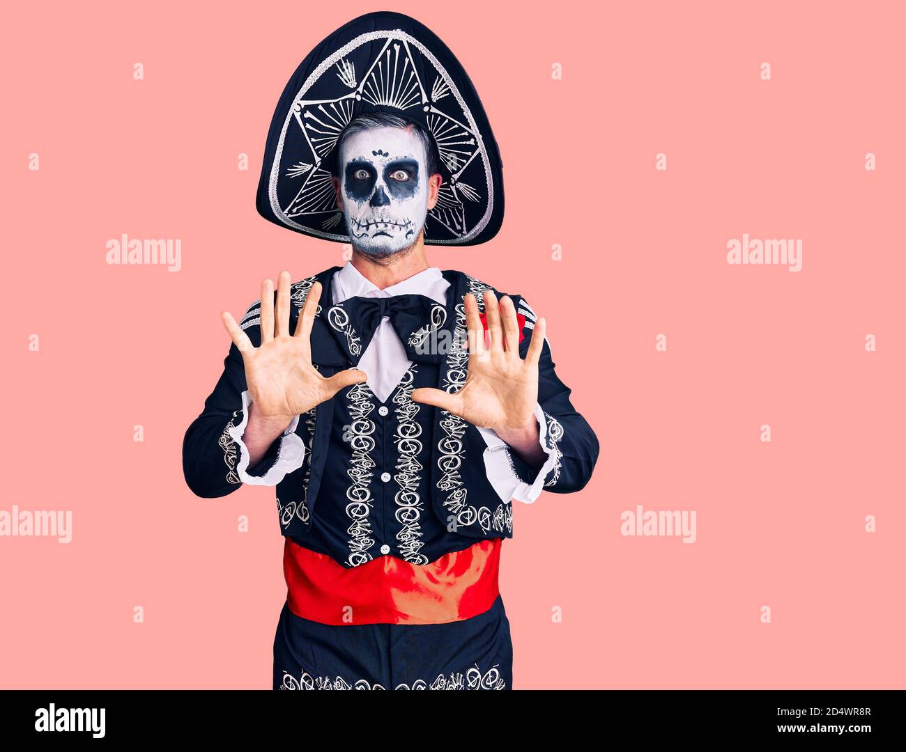 Young man wearing day of the dead costume over background afraid and ...
