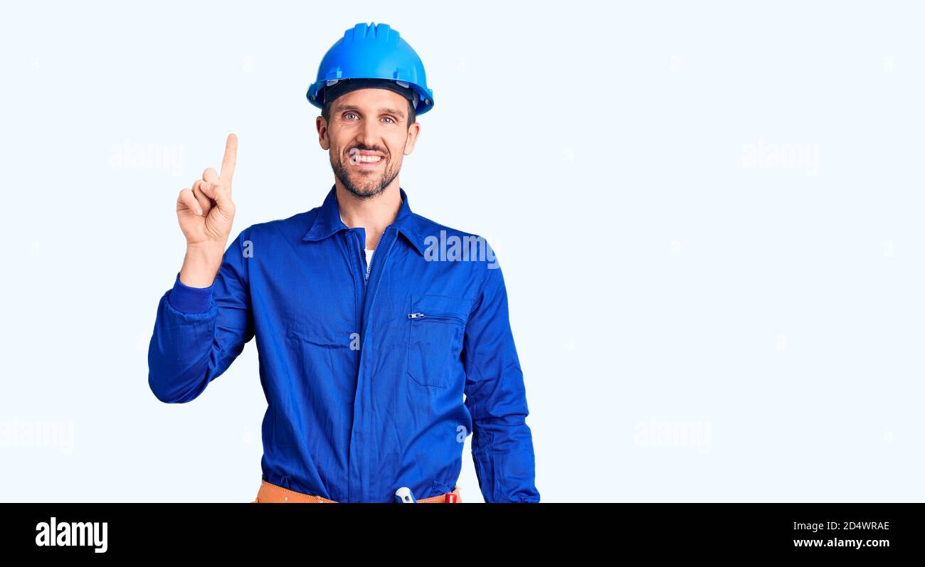 Young handsome man wearing worker uniform and hardhat pointing finger ...