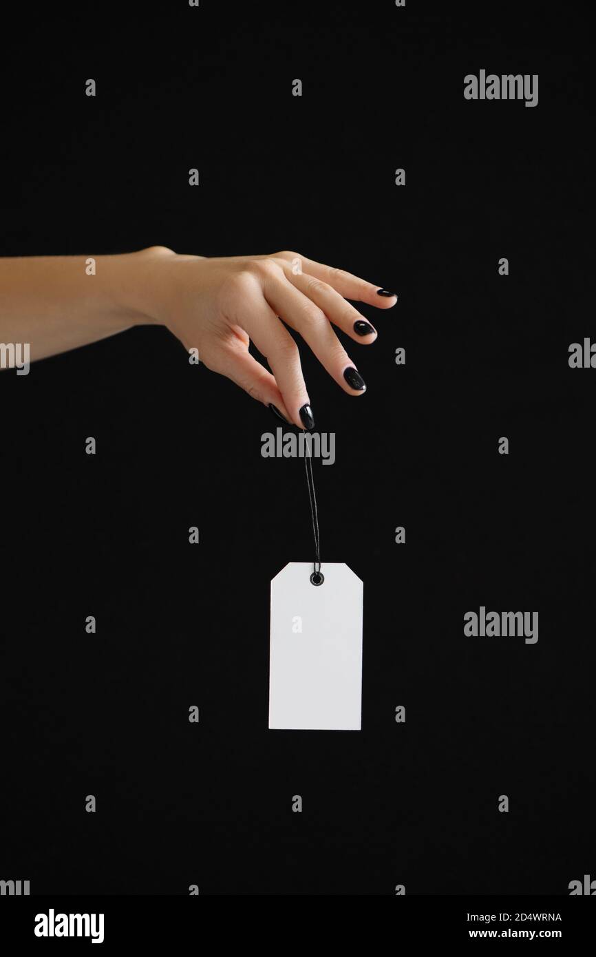 Woman hand holding white price tag on black background Stock Photo - Alamy