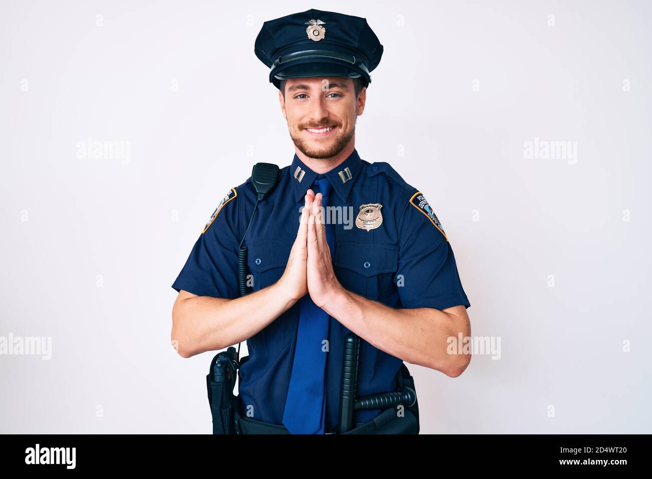 Young caucasian man wearing police uniform praying with hands together ...