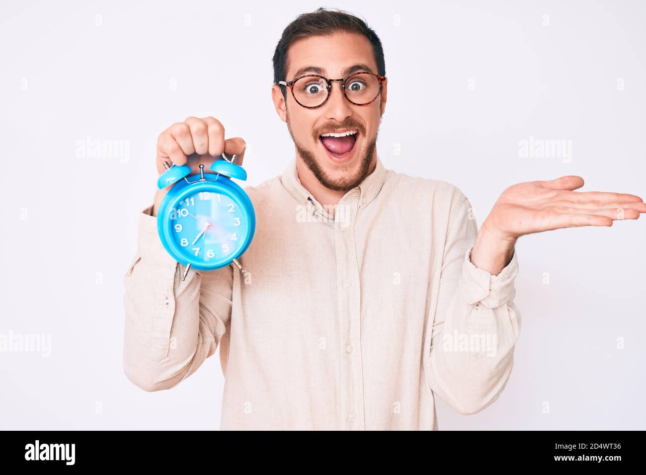 Young handsome man holding alarm clock celebrating achievement with ...
