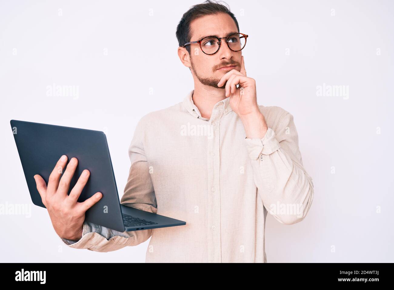 Young handsome man holding laptop serious face thinking about question ...