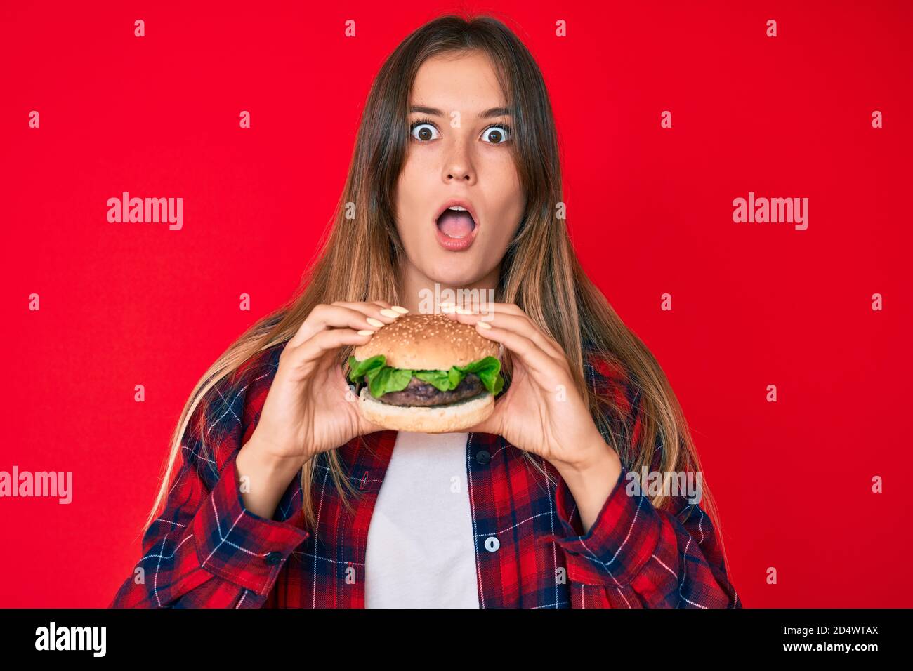 Beautiful caucasian woman eating a tasty classic burger afraid and ...