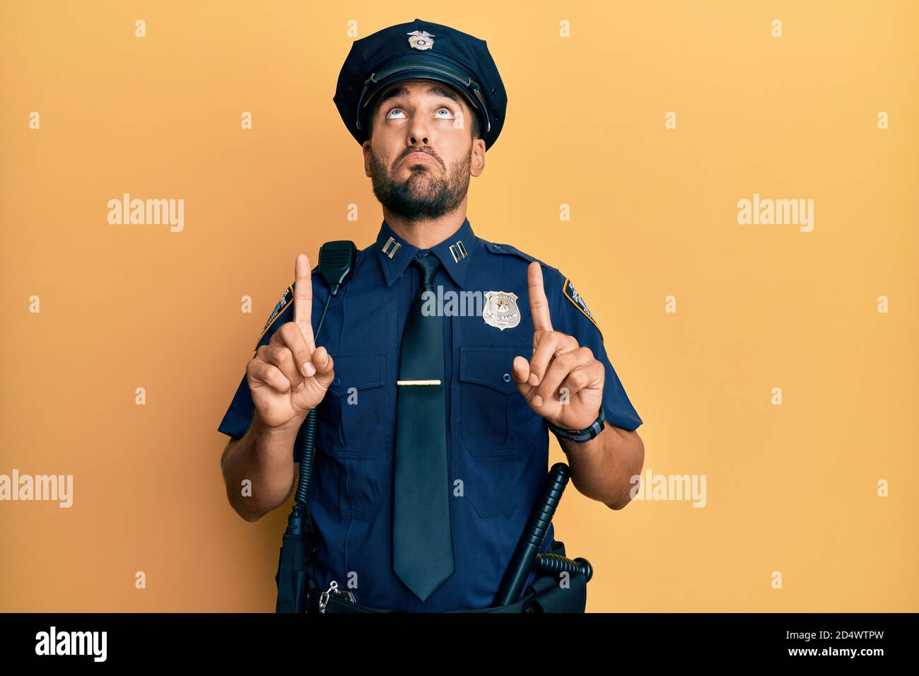 Handsome hispanic man wearing police uniform pointing up looking sad ...