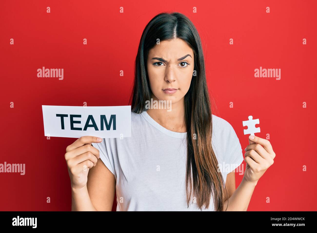 Young brunette woman holding team paper and piece of puzzle as teamwork ...
