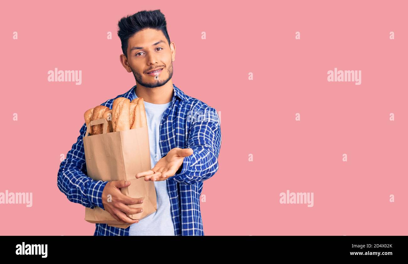 Handsome latin american young man holding paper bag with bread smiling ...
