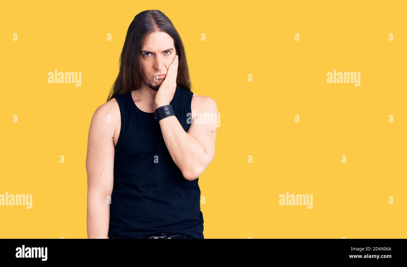 Young adult man with long hair wearing goth style with black clothes ...
