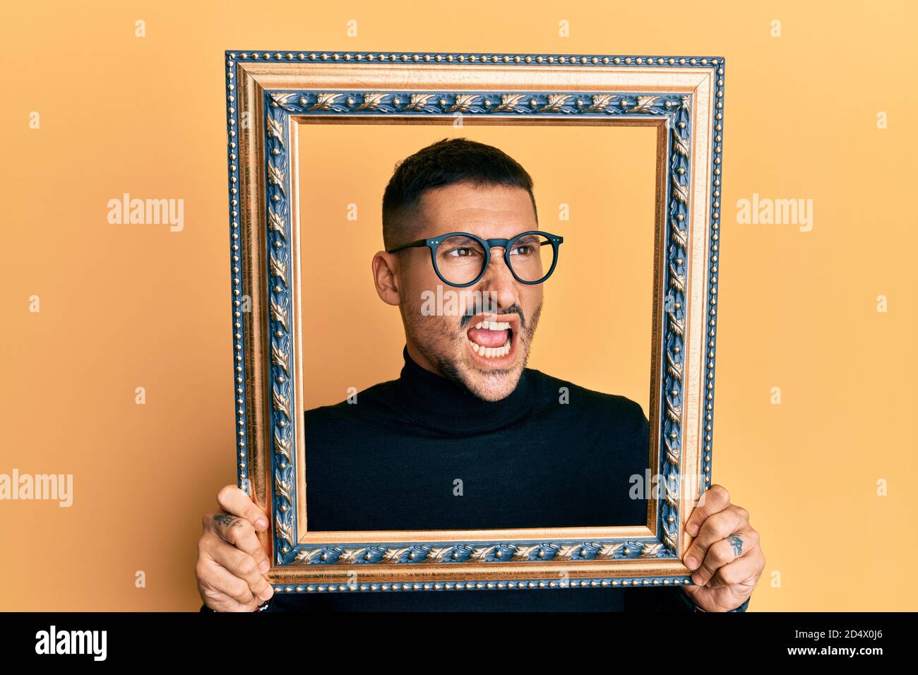 Handsome man with tattoos holding empty frame angry and mad screaming ...