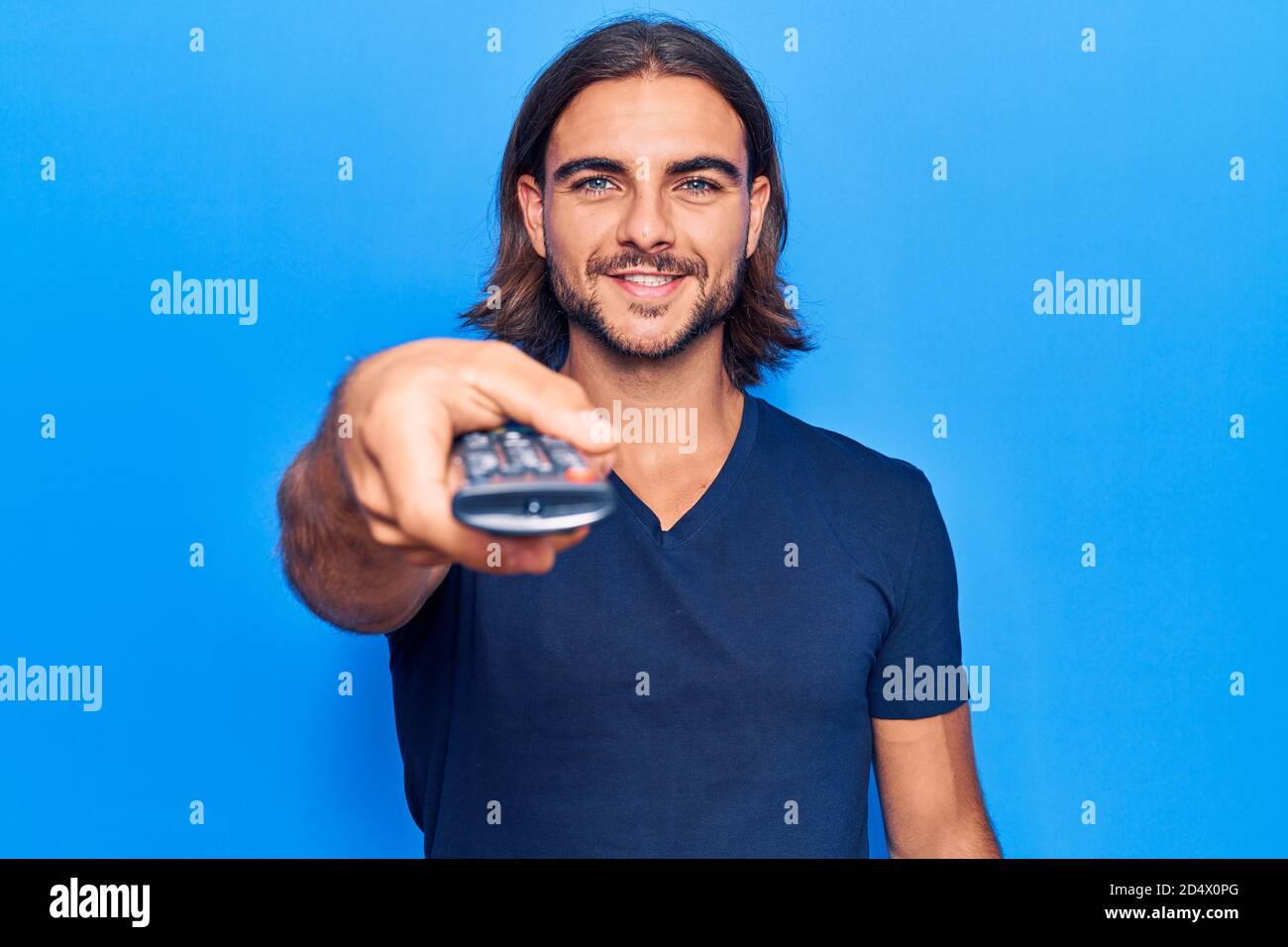 Young handsome man holding television remote control looking positive ...