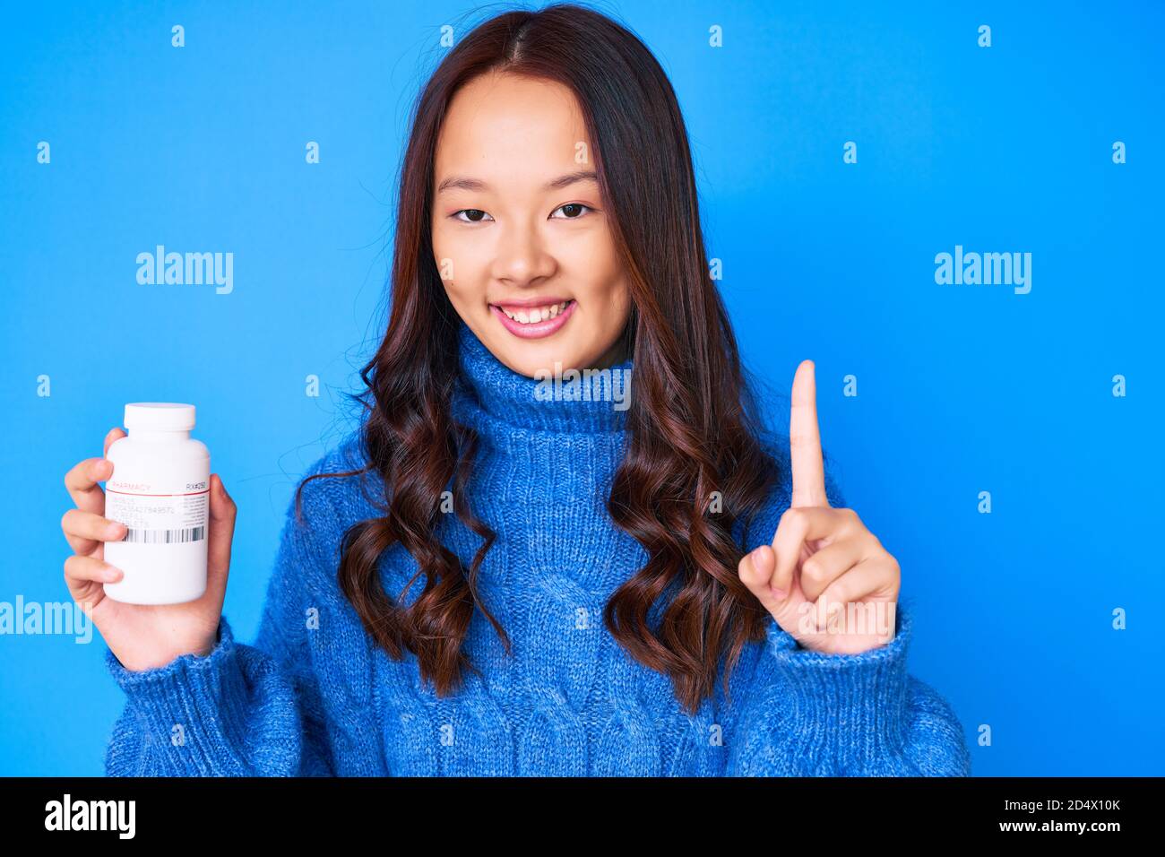 Young beautiful chinese girl holding pills smiling with an idea or ...