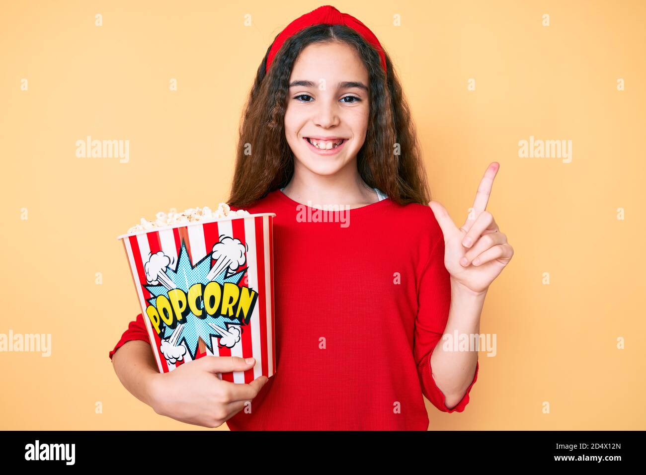 Cute hispanic child girl holding popcorn smiling happy pointing with ...