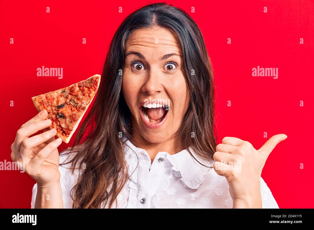 Young beautiful brunette woman eating slice of Italian pizza over ...