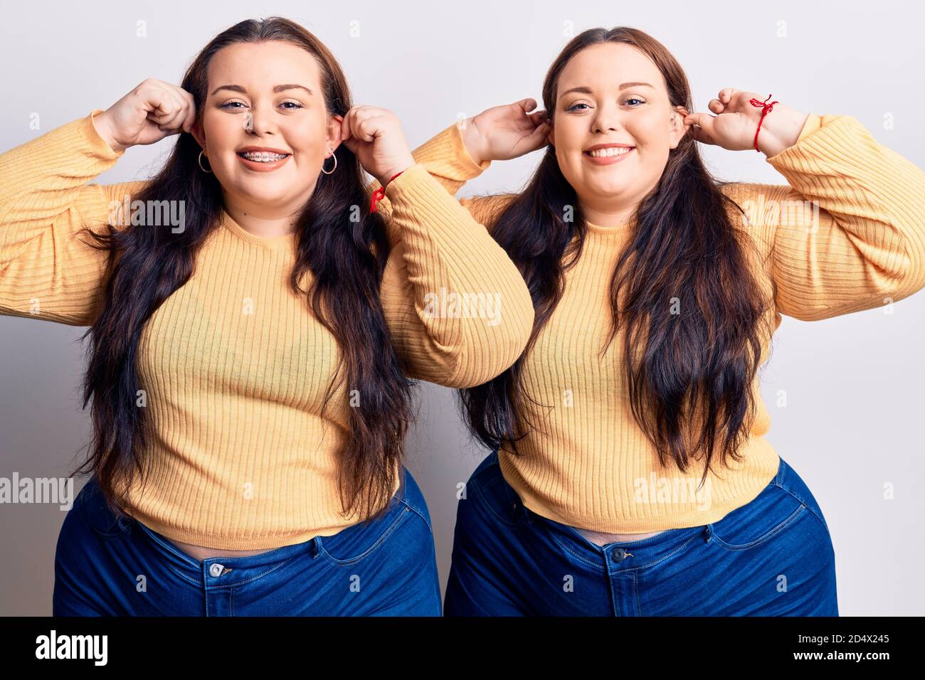 Young plus size twins wearing casual clothes smiling pulling ears with ...