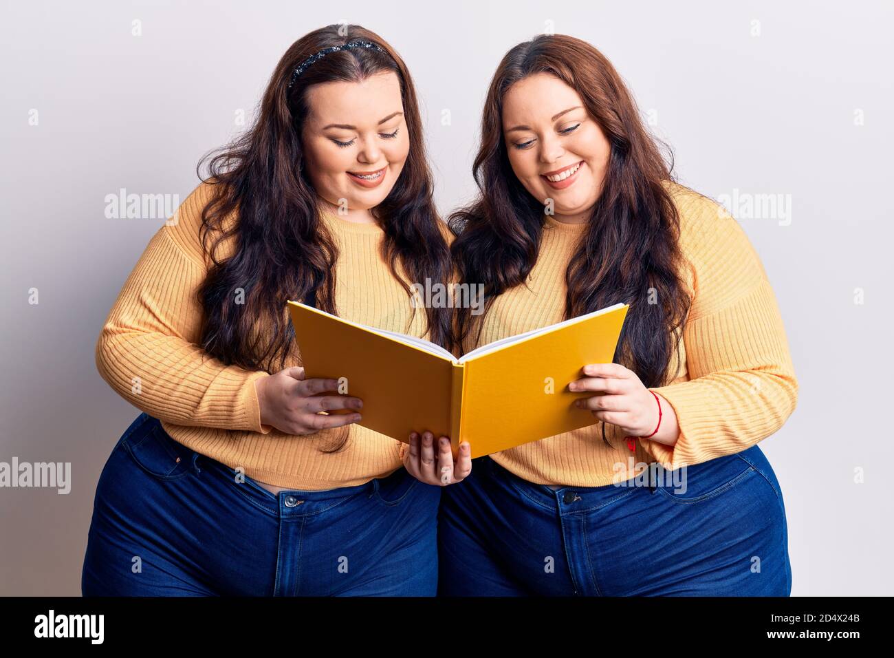 Young plus size twins holding book looking positive and happy standing ...