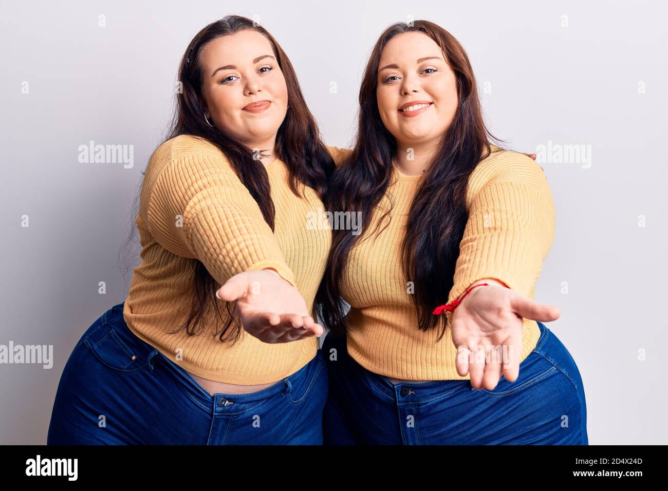 Young plus size twins wearing casual clothes smiling cheerful offering ...