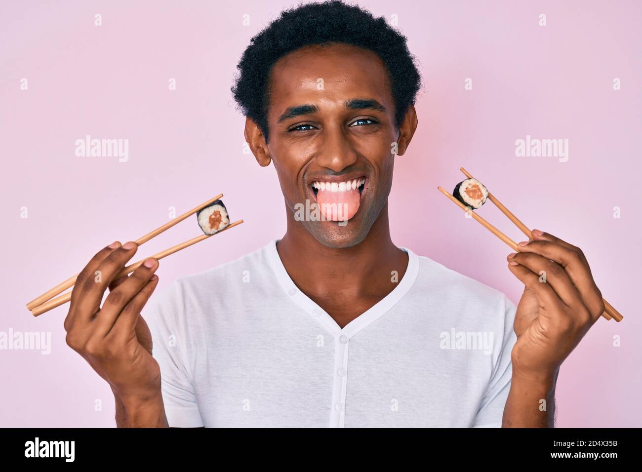 African handsome man eating sushi using chopsticks sticking tongue out ...