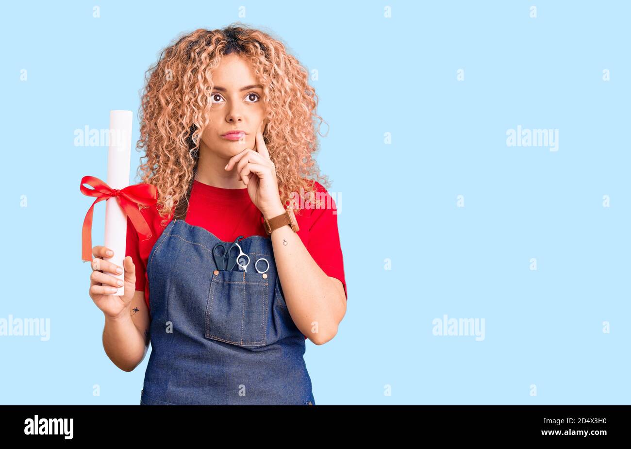 Young blonde woman with curly hair wearing hairdresser apron and ...